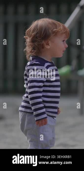 Toddler pausing in sand area at public playground during outdoor ...