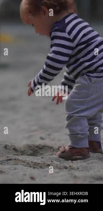 Toddler stepping across sandbox beside play equipment while wearing ...