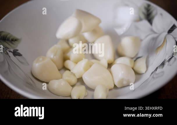 Freshly peeled garlic cloves gracefully tumble into a white floral ...
