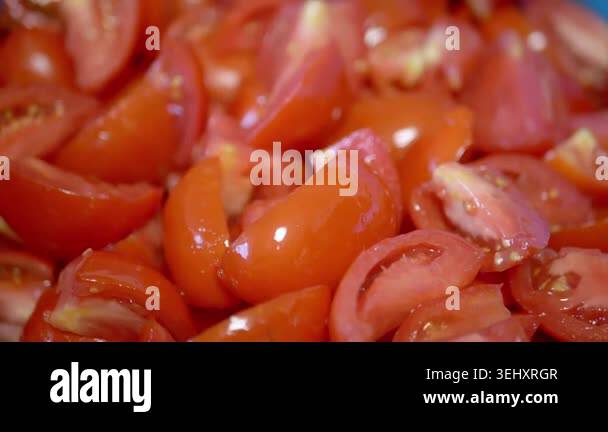 A female hand gently tosses juicy cut red tomatoes in a blue bowl ...