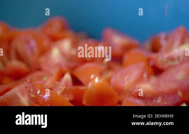 Fresh wedges of red tomatoes fall and tumble into a blue bowl in a ...