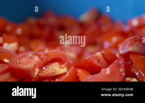 Fresh pieces of chopped red tomatoes fall into a blue bowl, creating a ...
