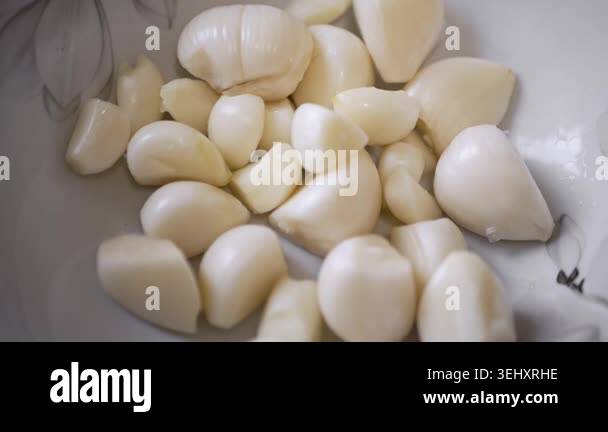 Close-up of fresh peeled garlic cloves piled in a white ceramic bowl ...