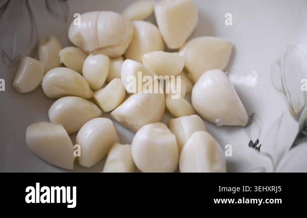 A heap of fresh peeled garlic cloves rests in a white ceramic bowl ...