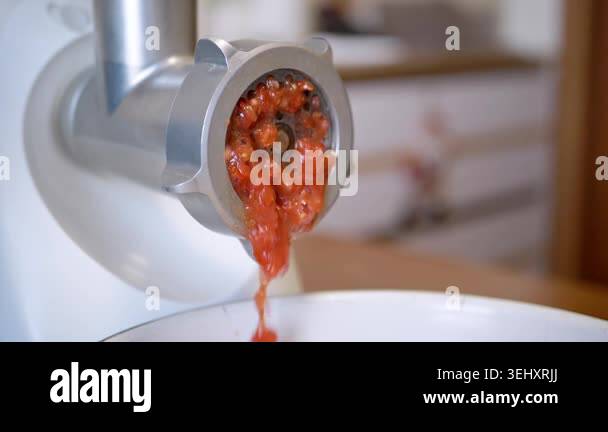 An electric grinder processes ripe red tomatoes into thick pulp with ...