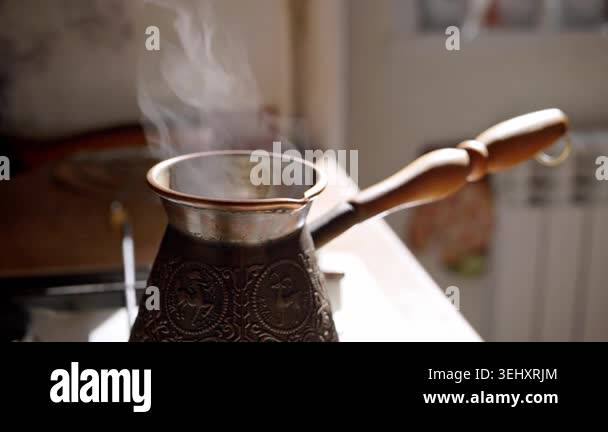 Steam rises from a traditional copper coffee pot with a wooden handle ...