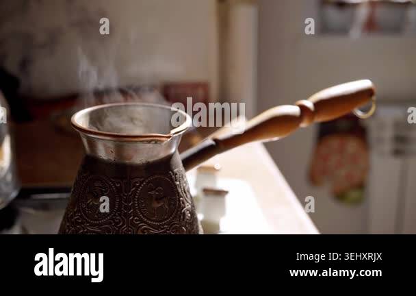 A traditional copper cezve sits on a stove with thick steam rising ...