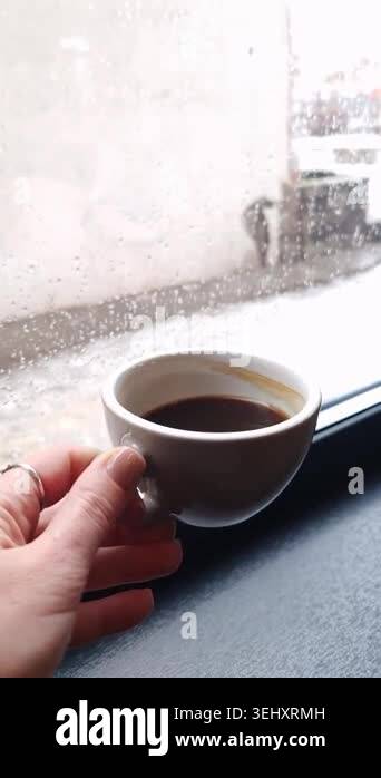 A hand with a ring holds a white ceramic cup of hot black coffee ...
