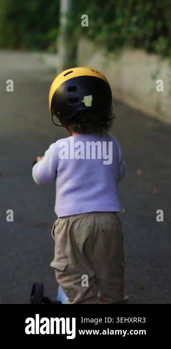 Small toddler riding scooter through calm neighborhood street while ...