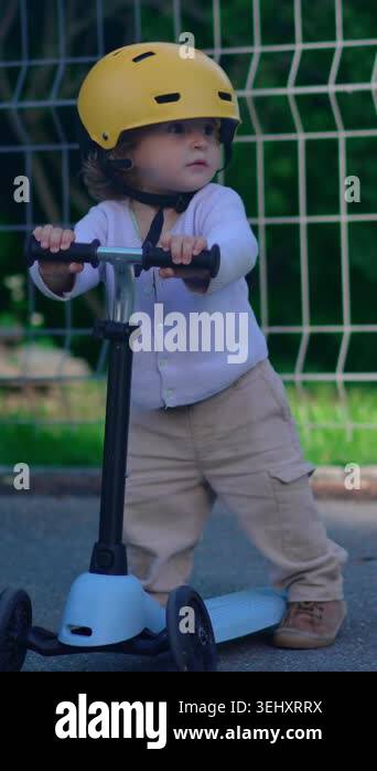Child stands balanced on scooter and looks into distance beside park ...