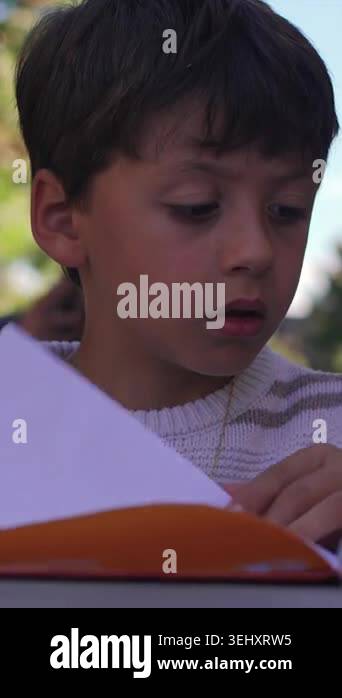 Child turning colorful book pages while relaxing outside on sunny day ...