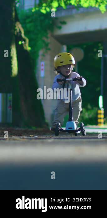 Toddler confidently approaches camera on scooter while exploring green ...