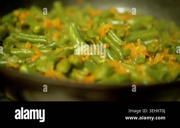 Fresh green beans and grated carrots simmer with steam rising in a hot ...