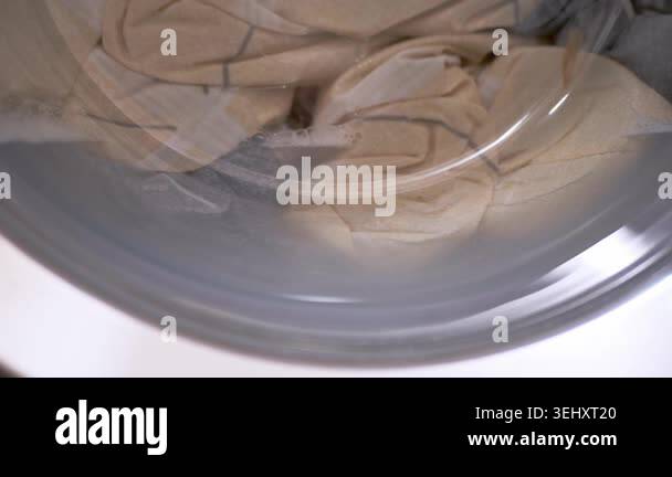Mixed laundry tumbles in soapy water inside the spinning drum of a ...
