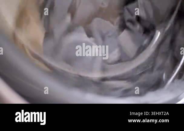 Wet garments tumble inside a spinning washing machine drum with ...