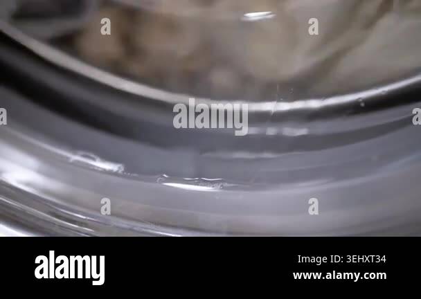 Wet laundry tumbles in splashing water behind the glass door of a ...