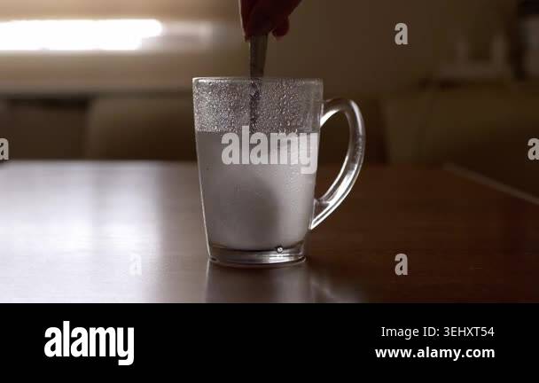 A person uses a spoon to stir a white effervescent tablet dissolving ...