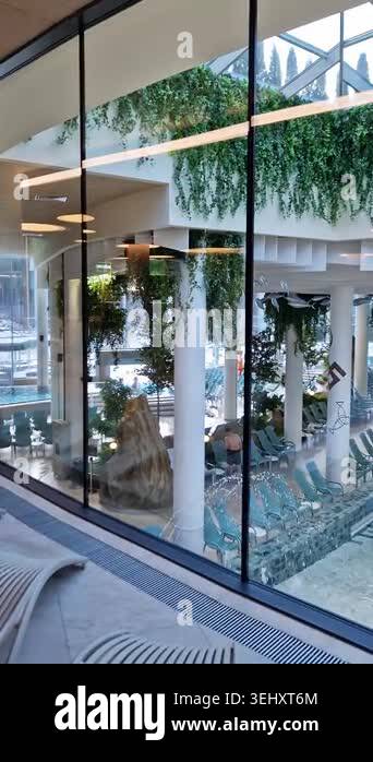 A vast indoor swimming pool complex showcases lush hanging plants and ...