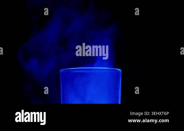 Thick blue smoke billows upwards from a clear glass tumbler set against ...