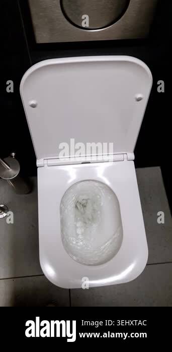 A close-up view captures swirling water inside a clean, modern toilet ...