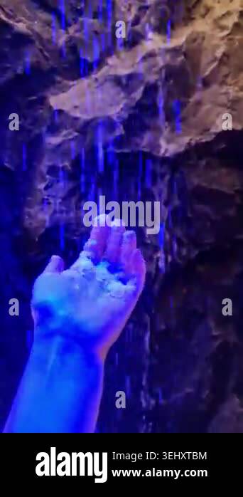 A hand reaches out to catch ice shavings falling from a fountain in a ...