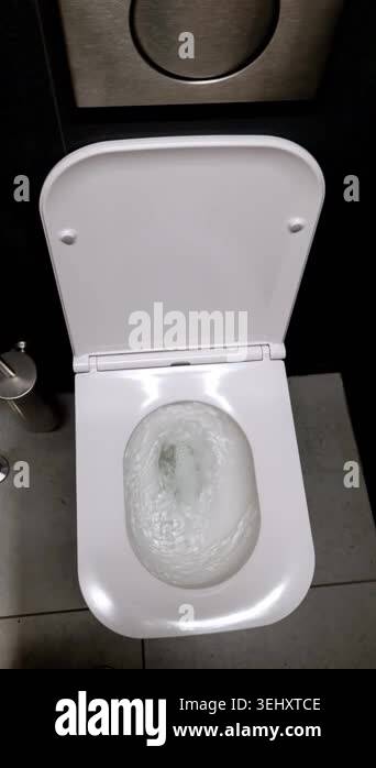A modern toilet bowl with water swirling rapidly down the drain during ...