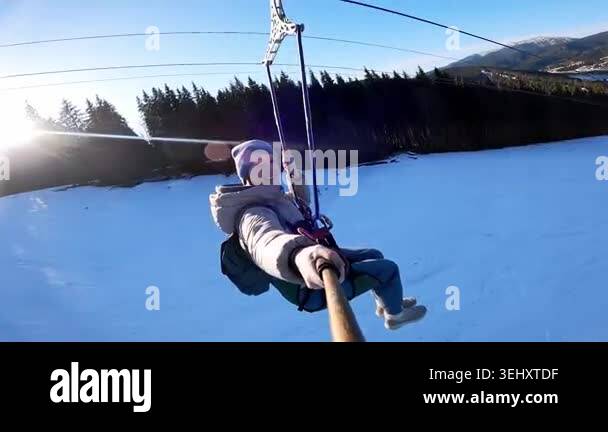 A smiling woman records her flight on an extreme zipline above a snowy ...