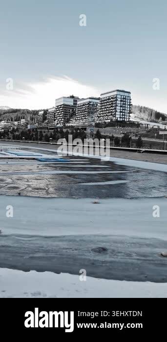 Wide shot of a partially frozen lake foreground, modern multi-story ...