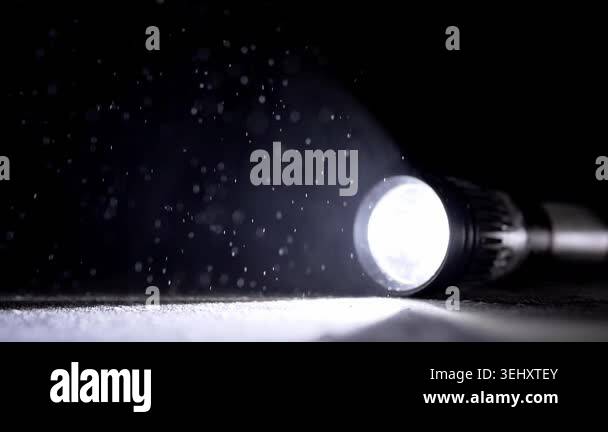 A tactical flashlight lies on a gritty surface, casting a sharp beam ...