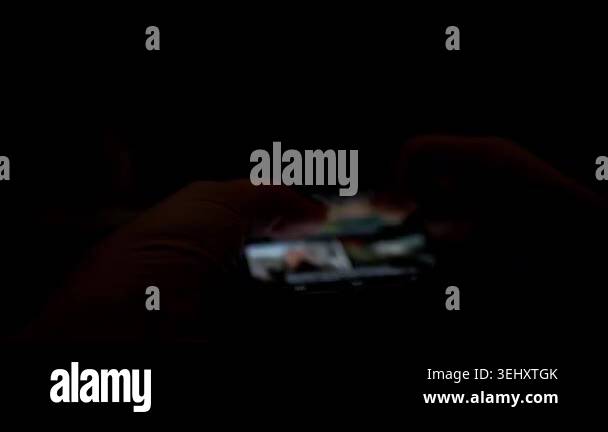 Close-up hands hold a smartphone while typing messages in a dark room ...