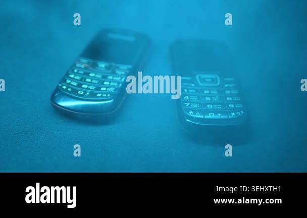 Two vintage black button mobile phones lie on a textured surface ...