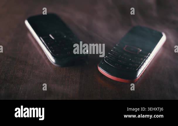 Two black keypad cell phones lie on a wooden surface as thick white ...