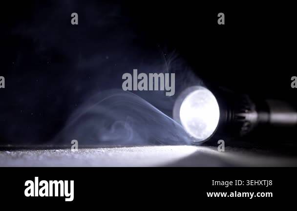 A tactical flashlight lies on a dark floor, projecting a bright beam ...