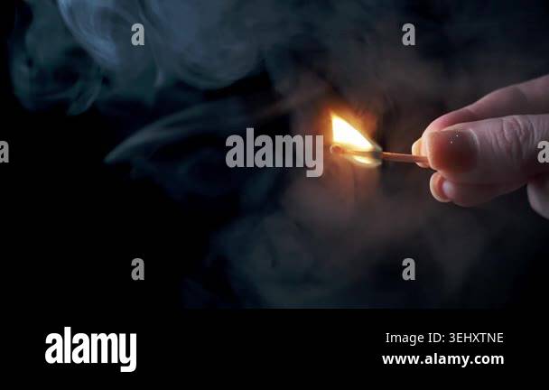 Fingers holding a burning matchstick while smoke gently swirls against ...