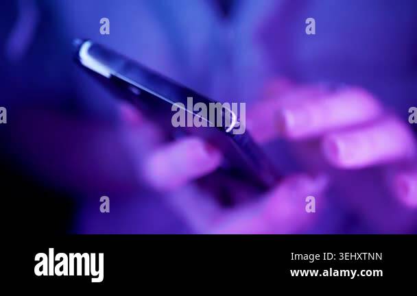 Close-up view of hands typing on a mobile phone screen illuminated by ...