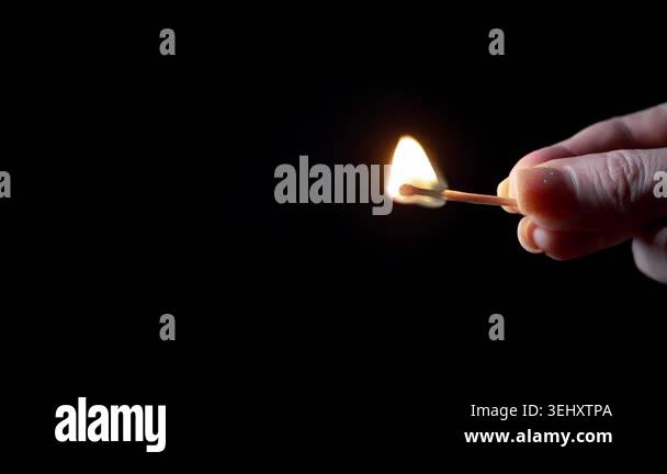 A close-up of a female hand holding a burning wooden match against a ...