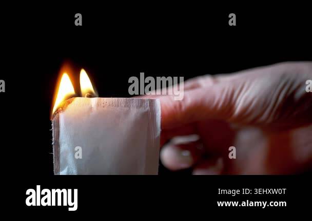 A person holds a white paper packet and uses a lit wooden match to ...
