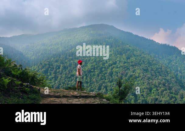 A person in a red cap and striped shirt stands on a rocky trail ...
