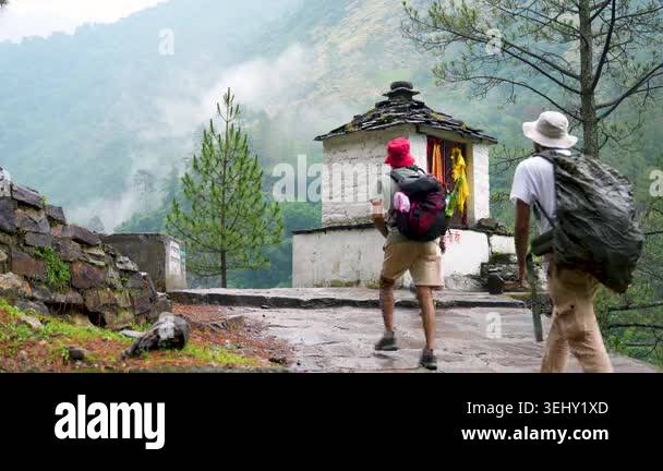 Two hikers with backpacks approach a traditional stone temple along a ...