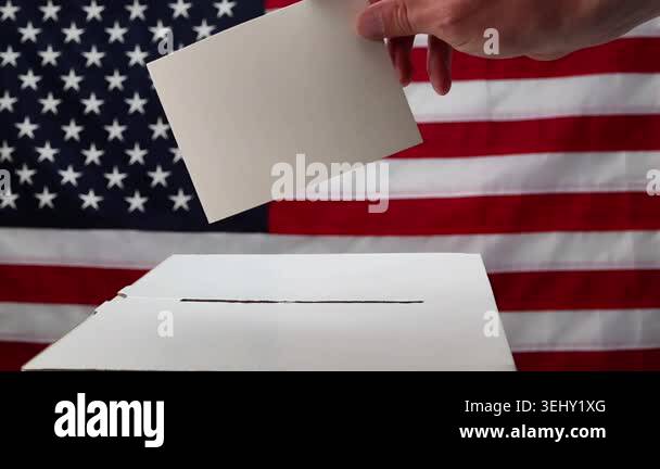 Hand placing voting ballot into a box in front of a united states flag ...