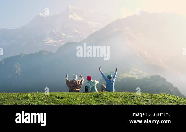 Three figures are seated on a green, grassy hill, gazing out at a vast ...