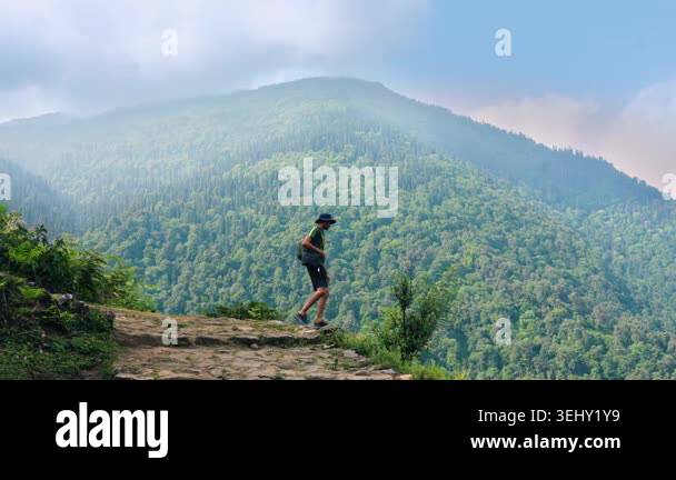 A person walks along a forested mountain path surrounded by dense ...