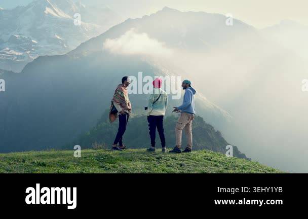 Three people stand on a grassy ridge, gazing at a vast, misty mountain ...