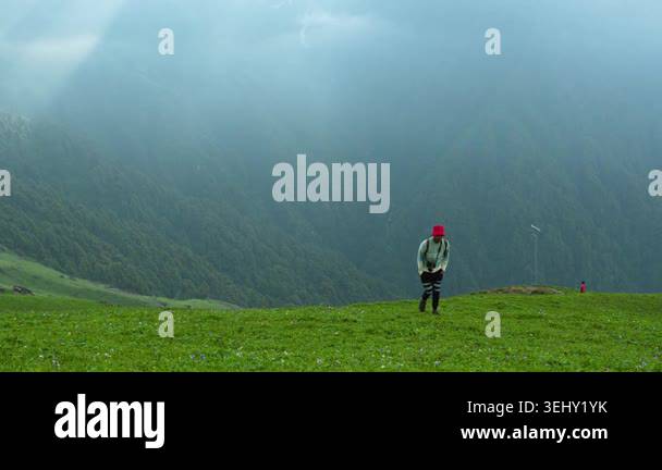A solitary figure in hiking gear pauses on a vibrant green meadow, with ...
