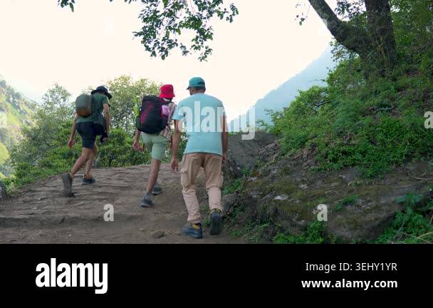 Three hikers walk along a rocky mountain path surrounded by greenery ...