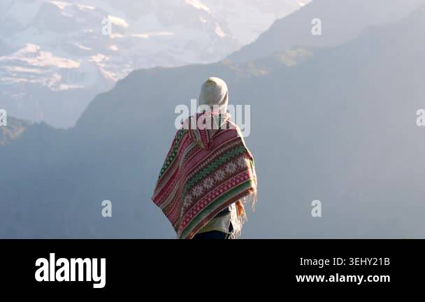A person wearing a colorful poncho and hood stands on a mountain ...