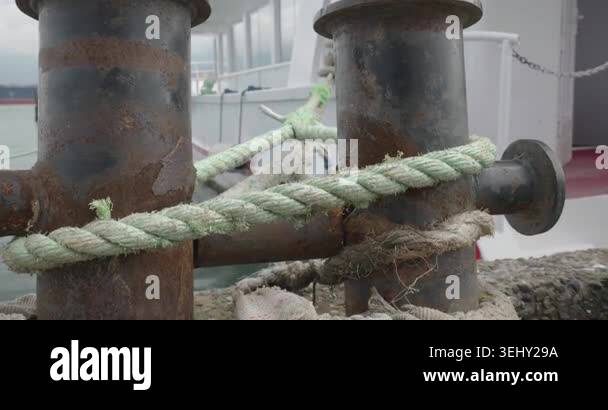 Close-up of weathered iron bollards and green rope with a blurred ship ...