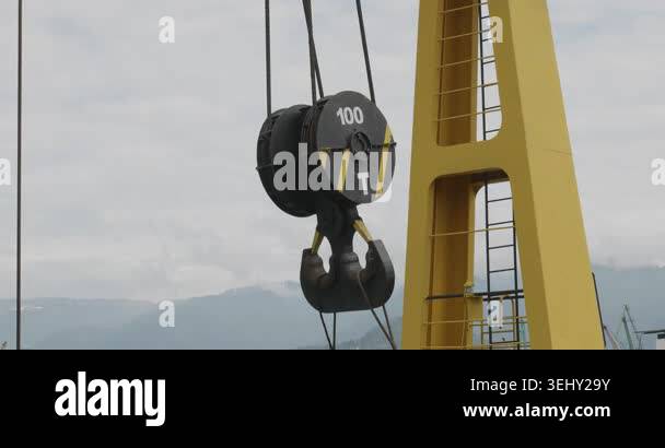 Close-up of a massive yellow port crane hook against a cloudy sky and ...