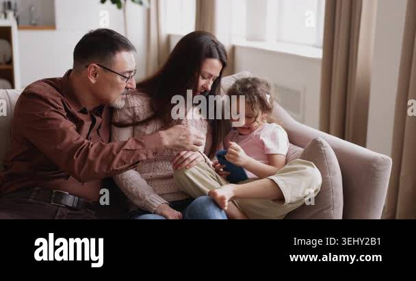 Loving parents sit on sofa with little child daughter holding modern ...
