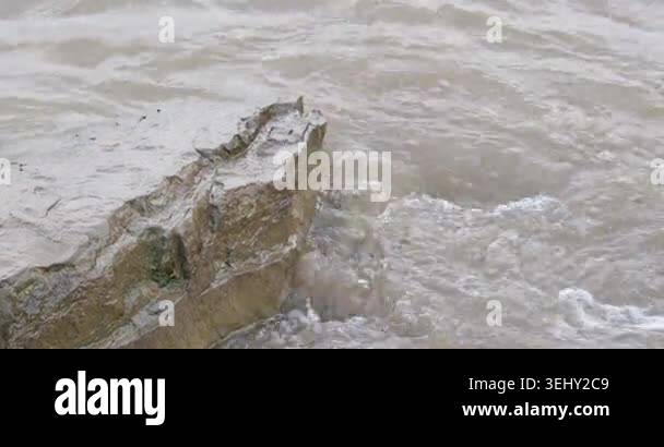 Close-up shot of fast-flowing, murky river water splashing against a ...